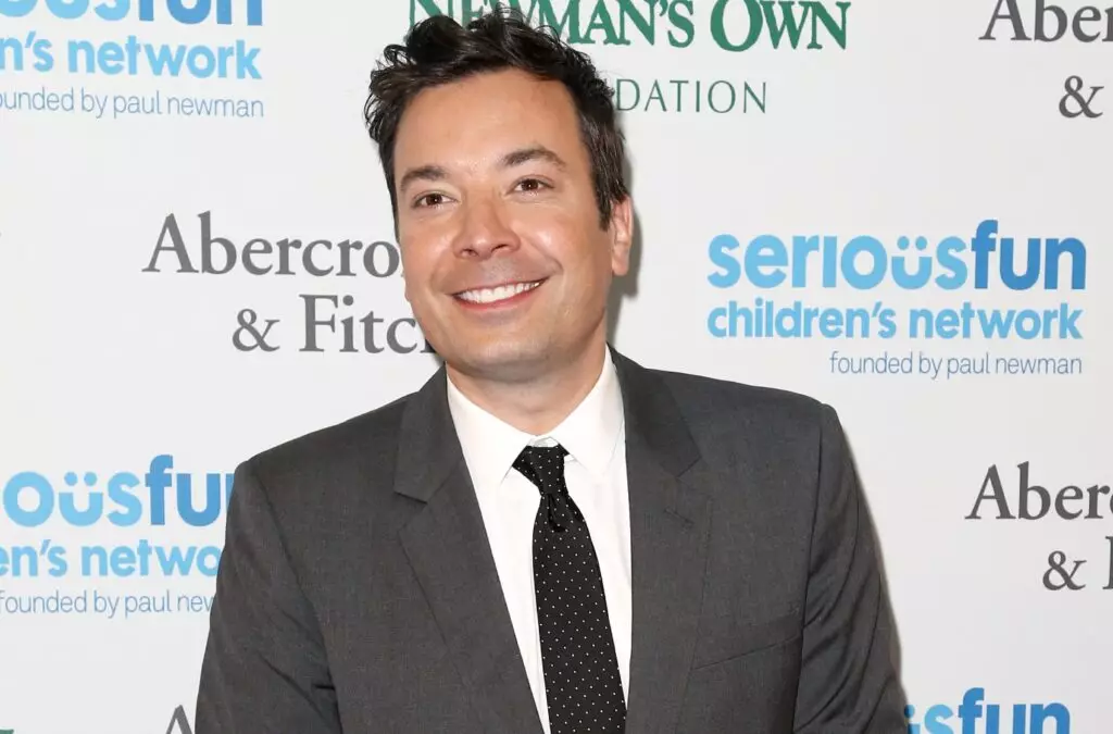 Jimmy Fallon vestindo um terno cinza e sorrindo.