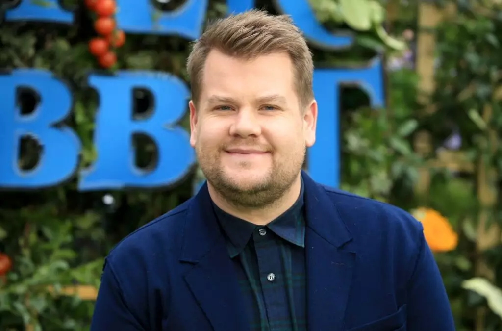 James Corden mesem lan nganggo jas biru.