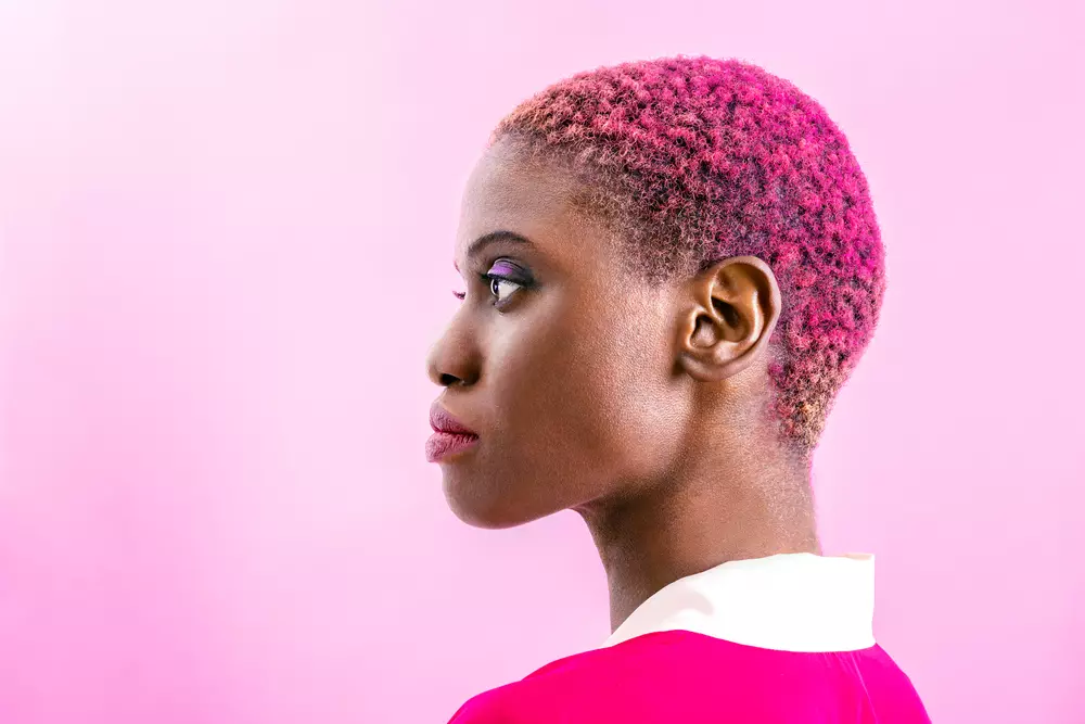 Ritratto di una donna dai capelli corti nera con i capelli rosa.