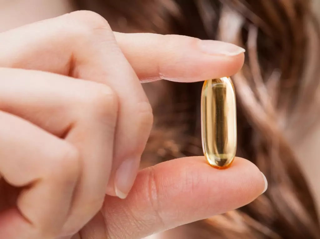 Close-up van vrouwenhand die Omega-3 capsule toont voor gezond haar, sterke nagels en glanzende huid