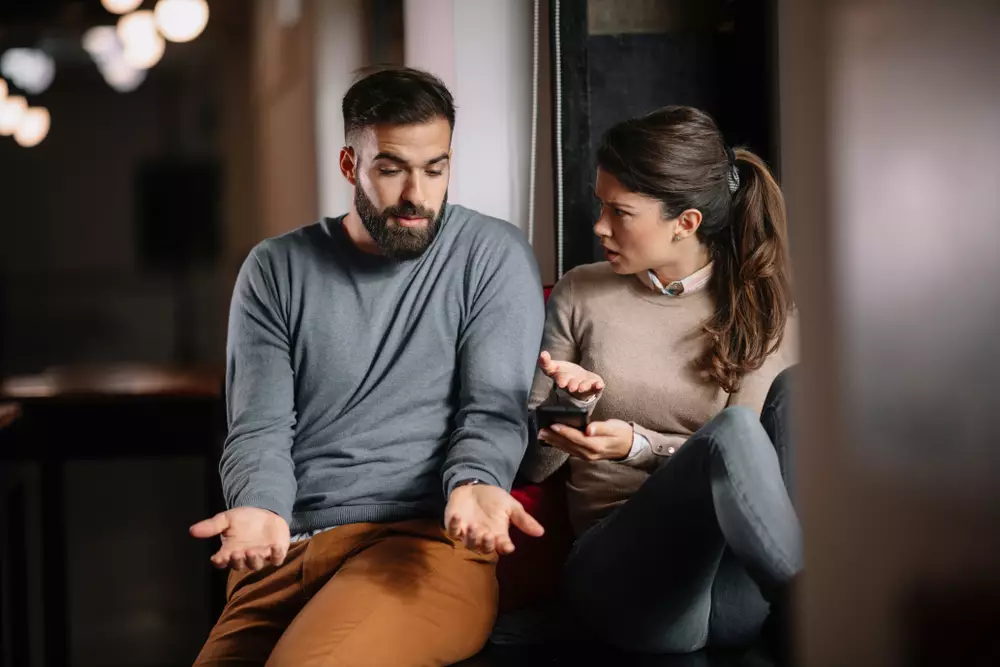 pasangan ambek atawa nikah pajoang pikeun handphone di imah. Awéwé Kaukasia sirik nyekel telepon pinter sareng nunjukkeun pesen ka salakina