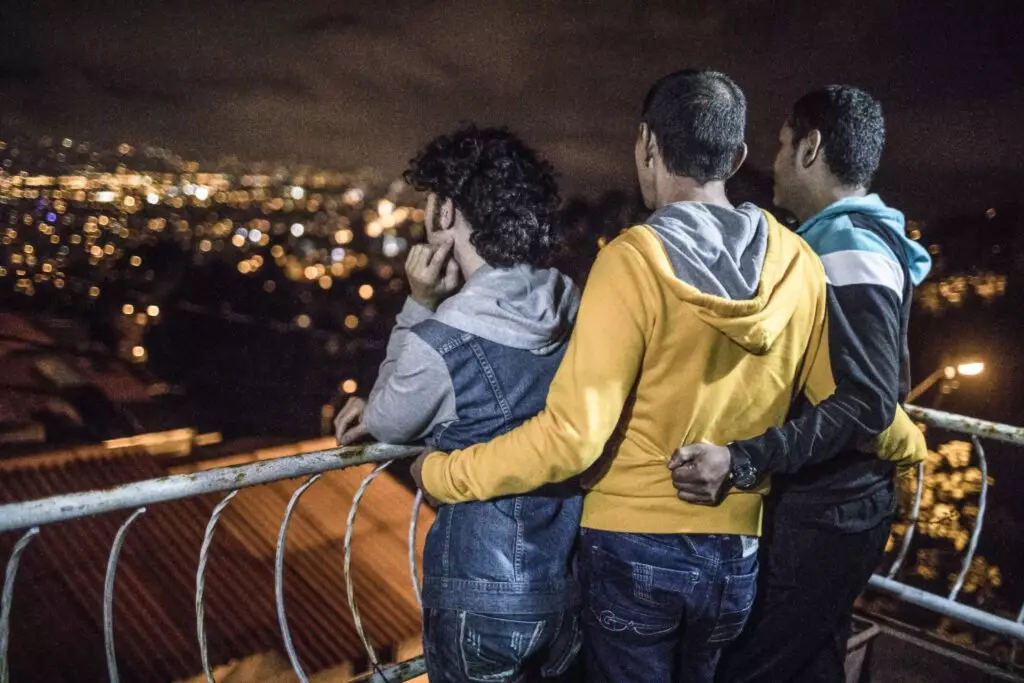 Mae Victor Prada (L), Alejandro Rodriguez (C), a Manuel Bermudez yn sefyll ar y balconi yn eu cartref yn Medellin, Colombia ar Fehefin 17, 2017. Mae'r tri dyn wedi ennill cydnabyddiaeth gyfreithiol fel y cyntaf